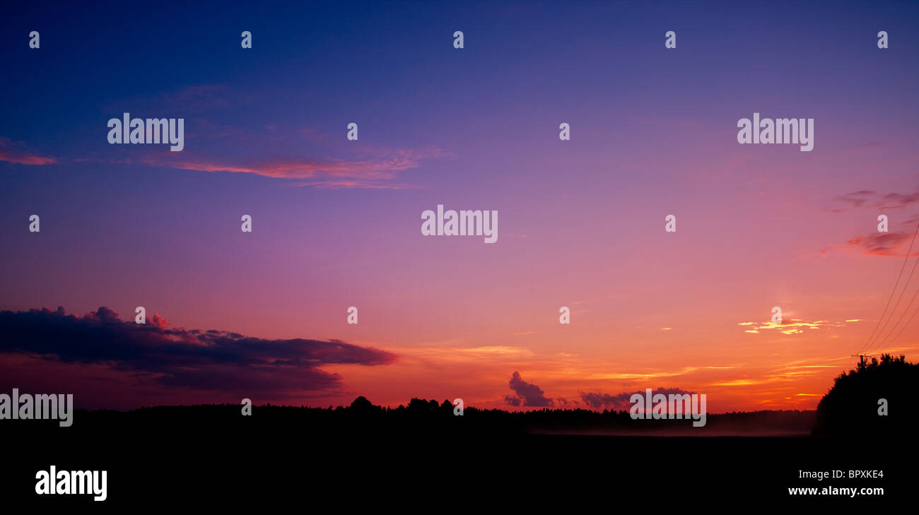August sunset with vivid colors and clouds, with fog and forest in the ...