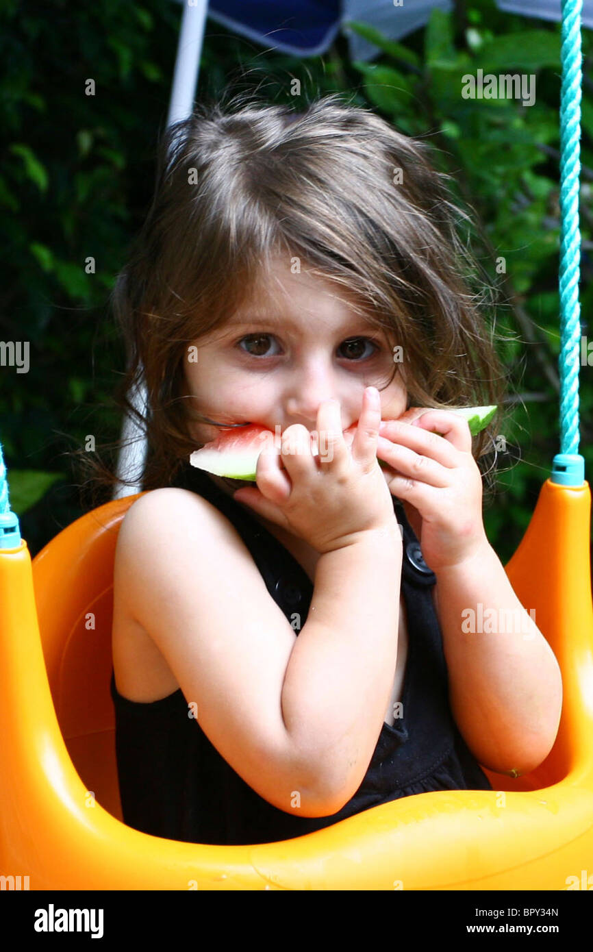 Young girl of three sits in a swing and eats a watermelon Stock Photo ...