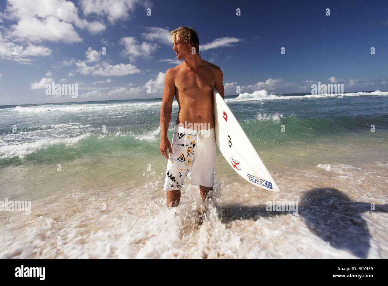 Young surfer with surfboard in Pacific Ocean on the North Shore of Oahu ...