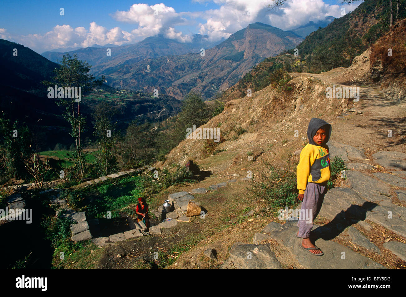 A young boy of about 9 years of age stands on a track in the Himalayan ...