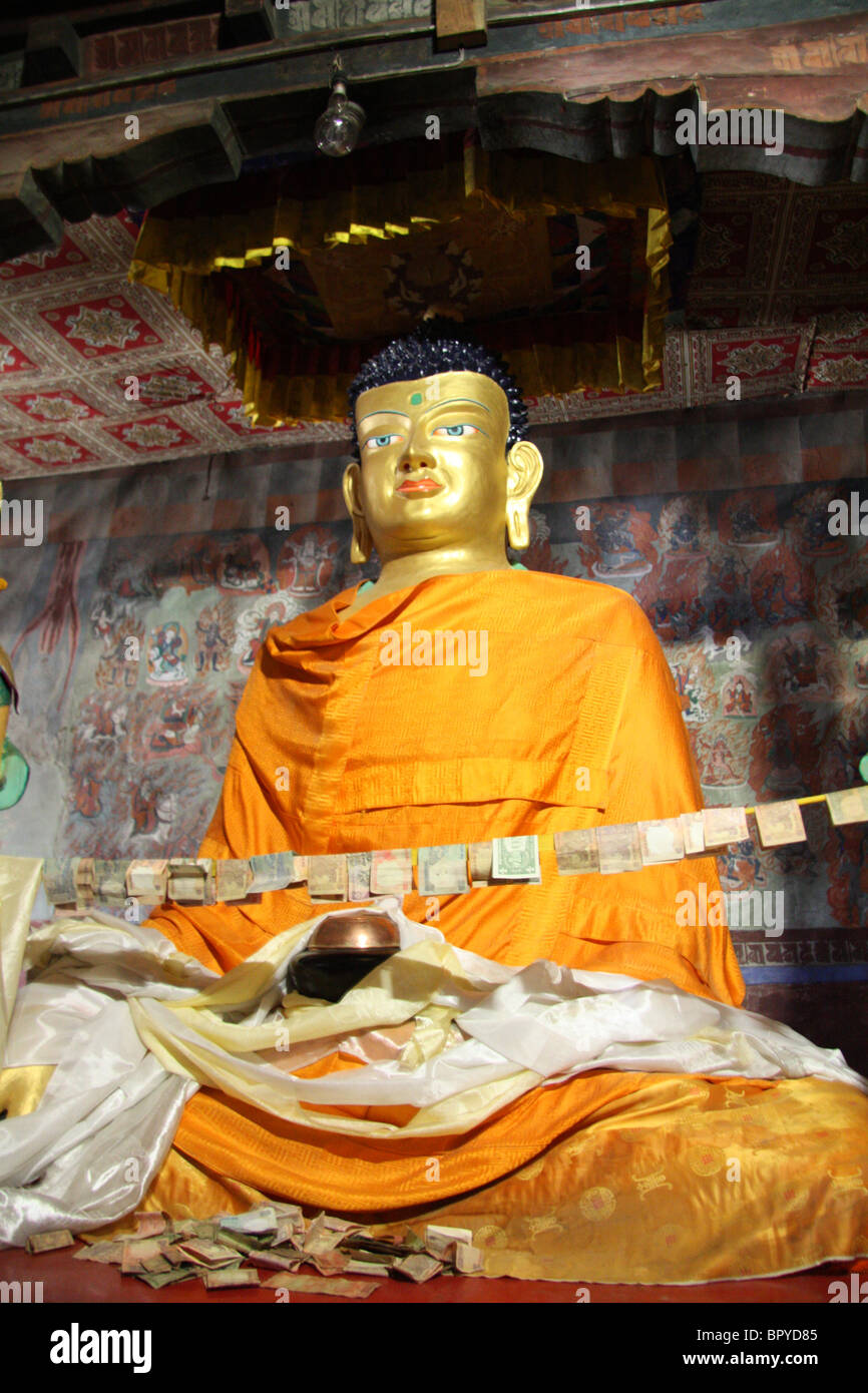 Seated, orange-robed Buddha statue with rupee offerings strung across ...