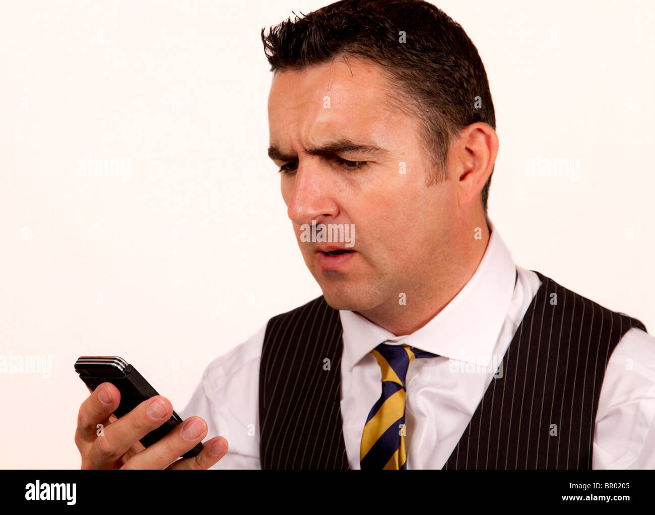 A businessman stares at his mobile phone, he looks confused and a ...