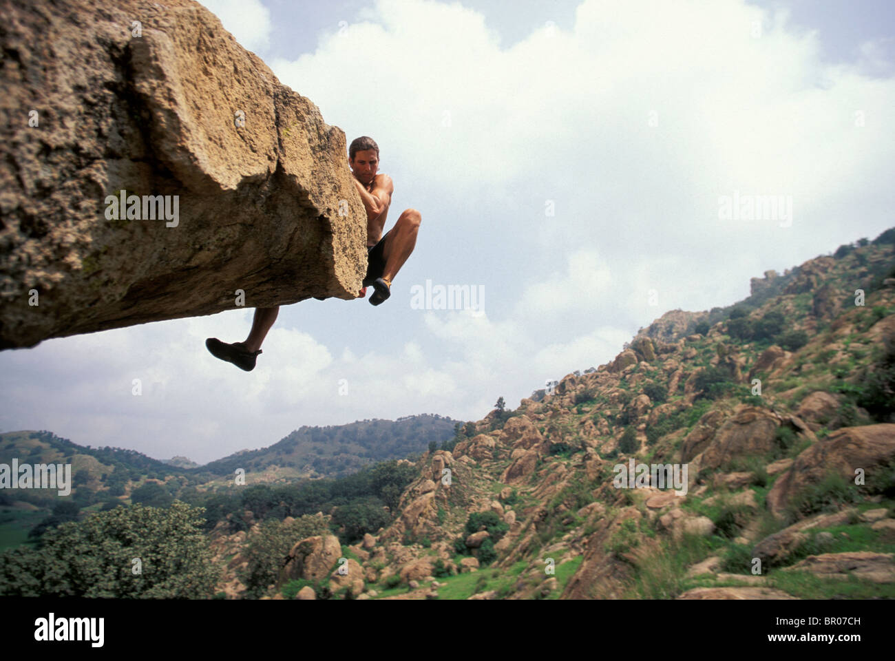 A male rock climber attempts to get over the top of an overhanging ...