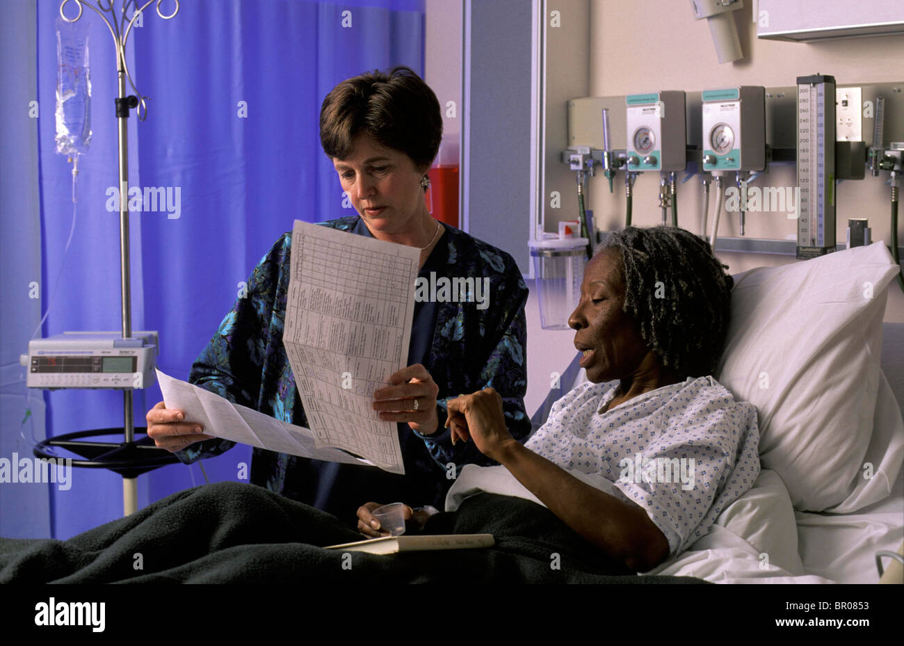 A doctor talks with her patient who is lying in a hospital bed ...