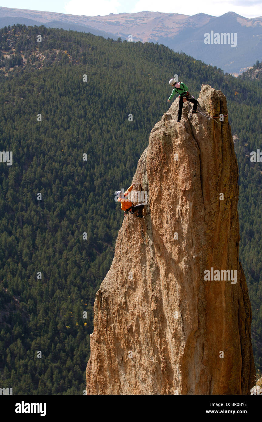 Two men climbing rock spire above forest Stock Photo - Alamy