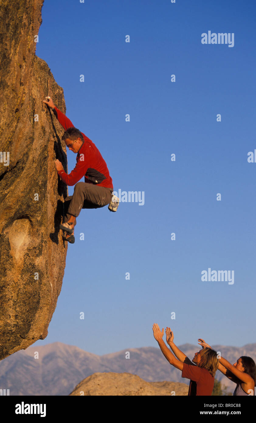 Two rock climbers spot a man climbing on a bouldering route in the ...