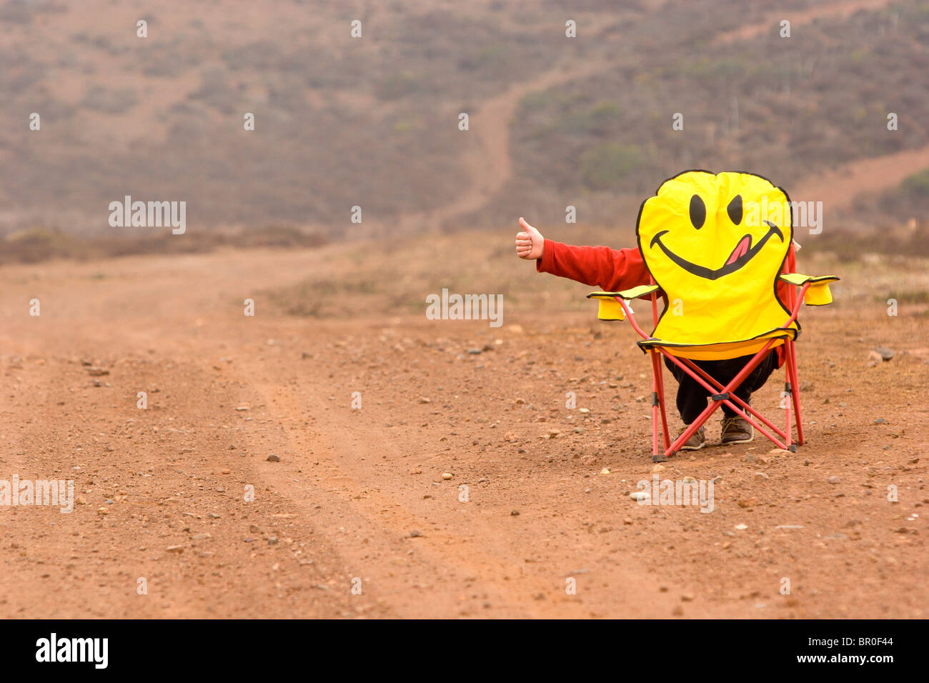 Young man hitch hiking behind happy face chair in Baja Norte, Mexico ...