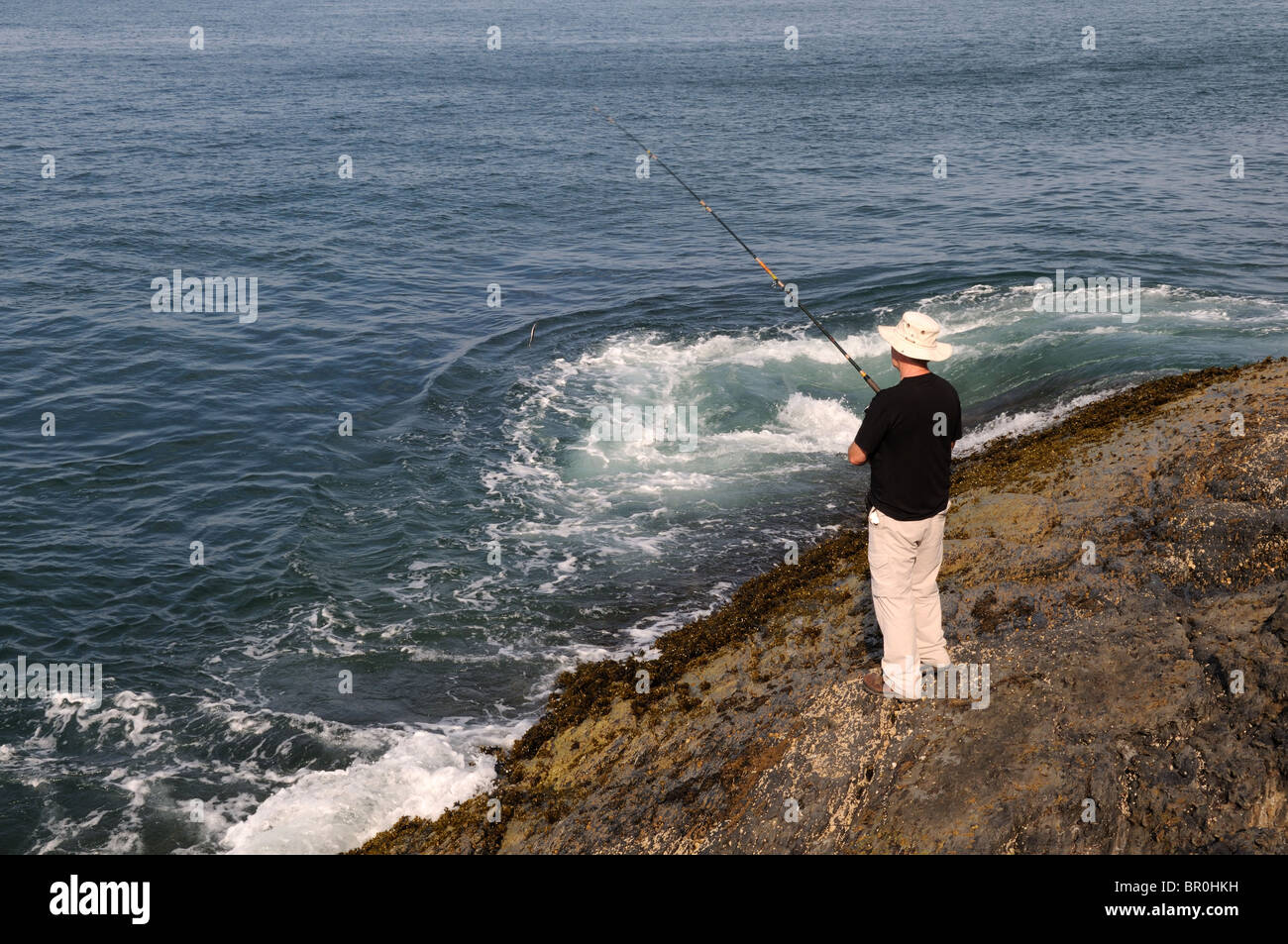 Man fishing off rocks near Mwnt Cardigan Bay Coastal Path Ceredigion ...
