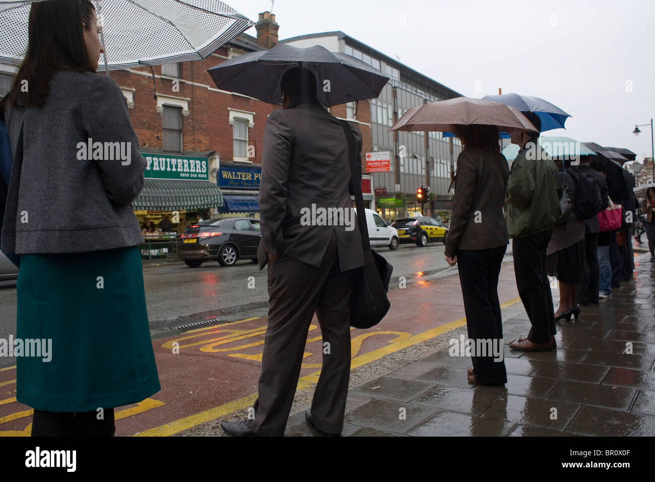 Commuters queue in the rain at a London bus stop Stock Photo - Alamy