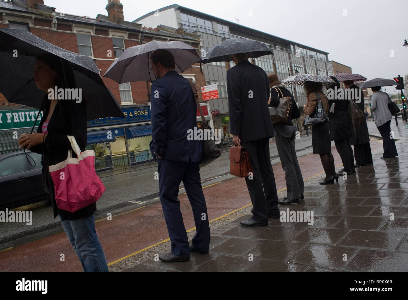 Morning commuters queue in the rain at a bus stop in London Stock Photo ...