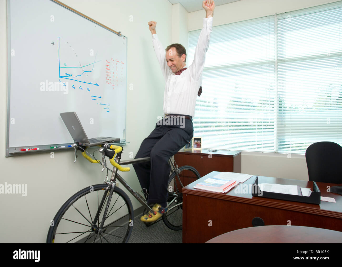 Corporate executive works out on his bicycle trainer as he works in his ...