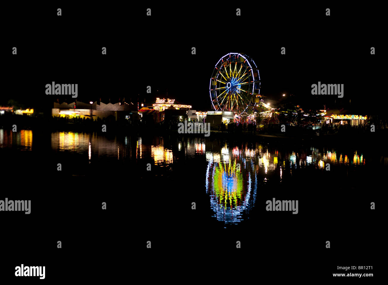 Nighttime Carnival Reflection. Fairgoers mill about a traveling ...