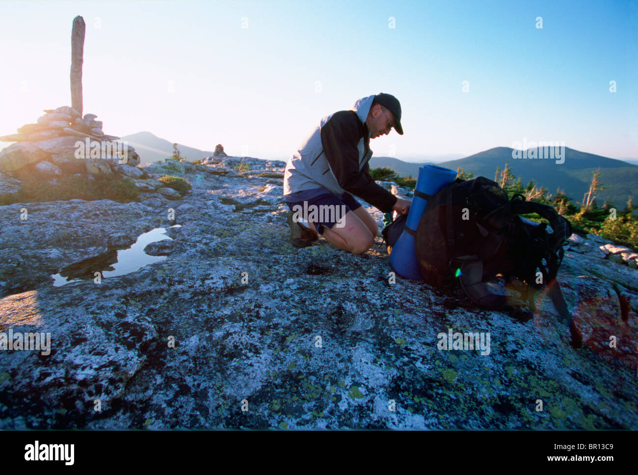 A hiker closes the top of his backpack before leaving a mountain summit ...