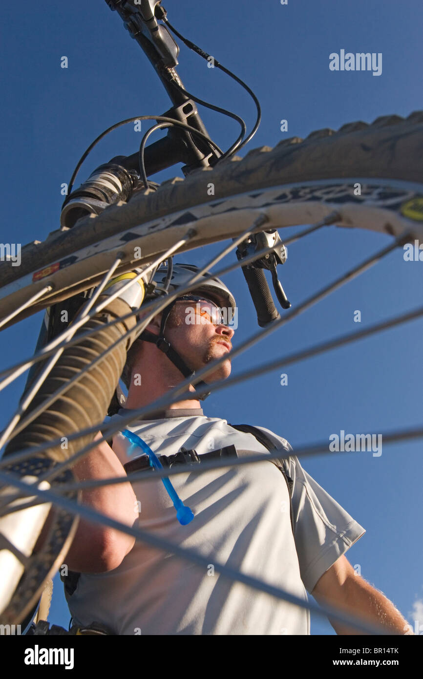 A portrait of a man through the mountain bike wheel that he is carrying ...