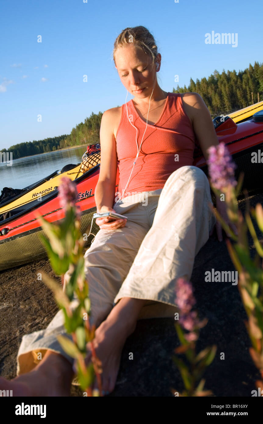 A woman listening to music on her iPod on an island in the Saimaa lake ...