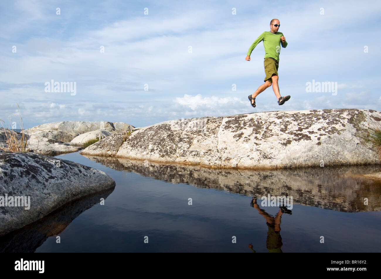 A man running along a rocky ridge above a small pond on one of the ...