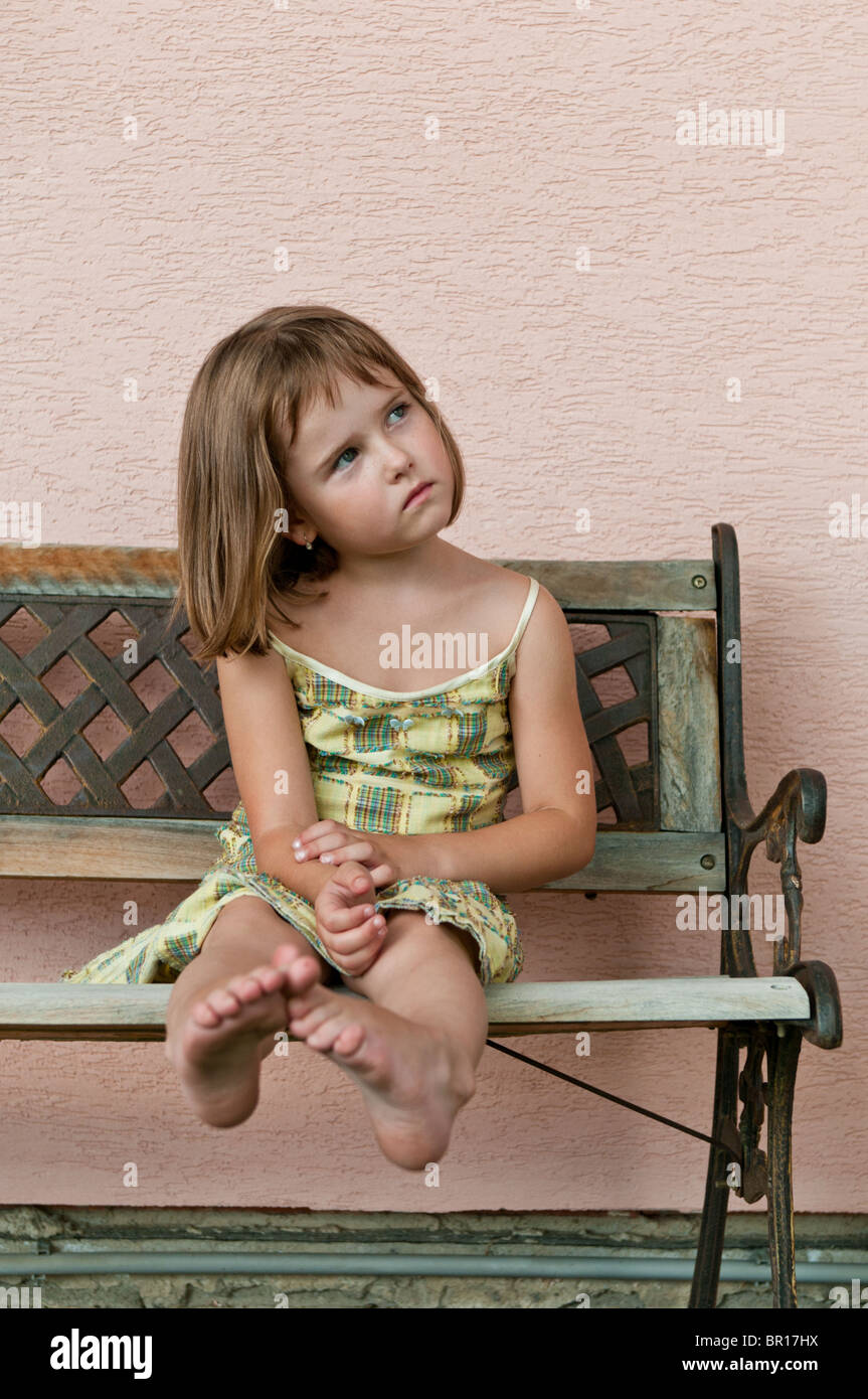 Portrait of cute child sitting on bench and stretching barefoot legs ...