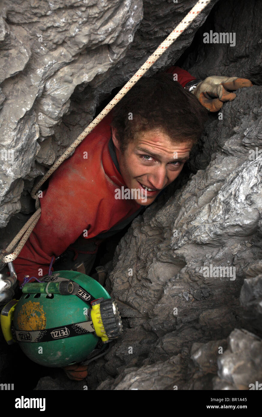 A cave explorer has to remove his helmet in order to pass the tight ...