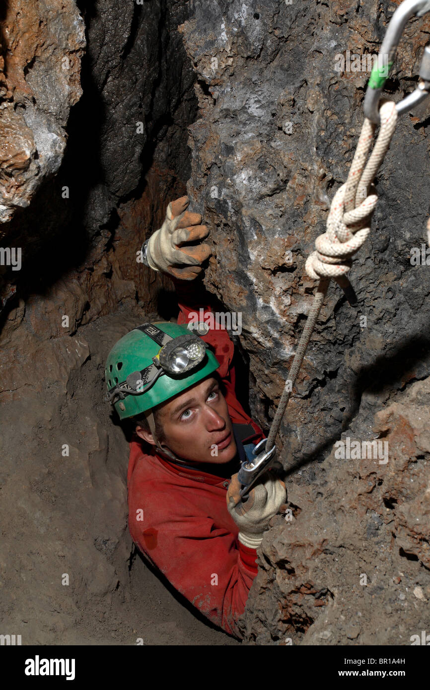 Cave explorer forces his way up through a narrowing in the rock in a ...
