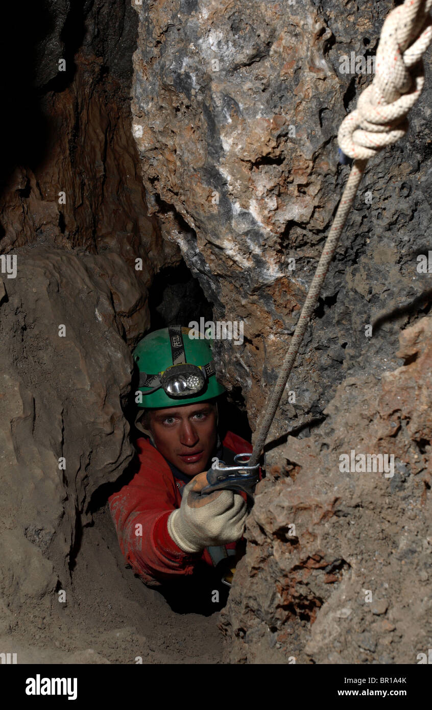 Cave explorer forces his way up through a narrowing in the rock in a ...