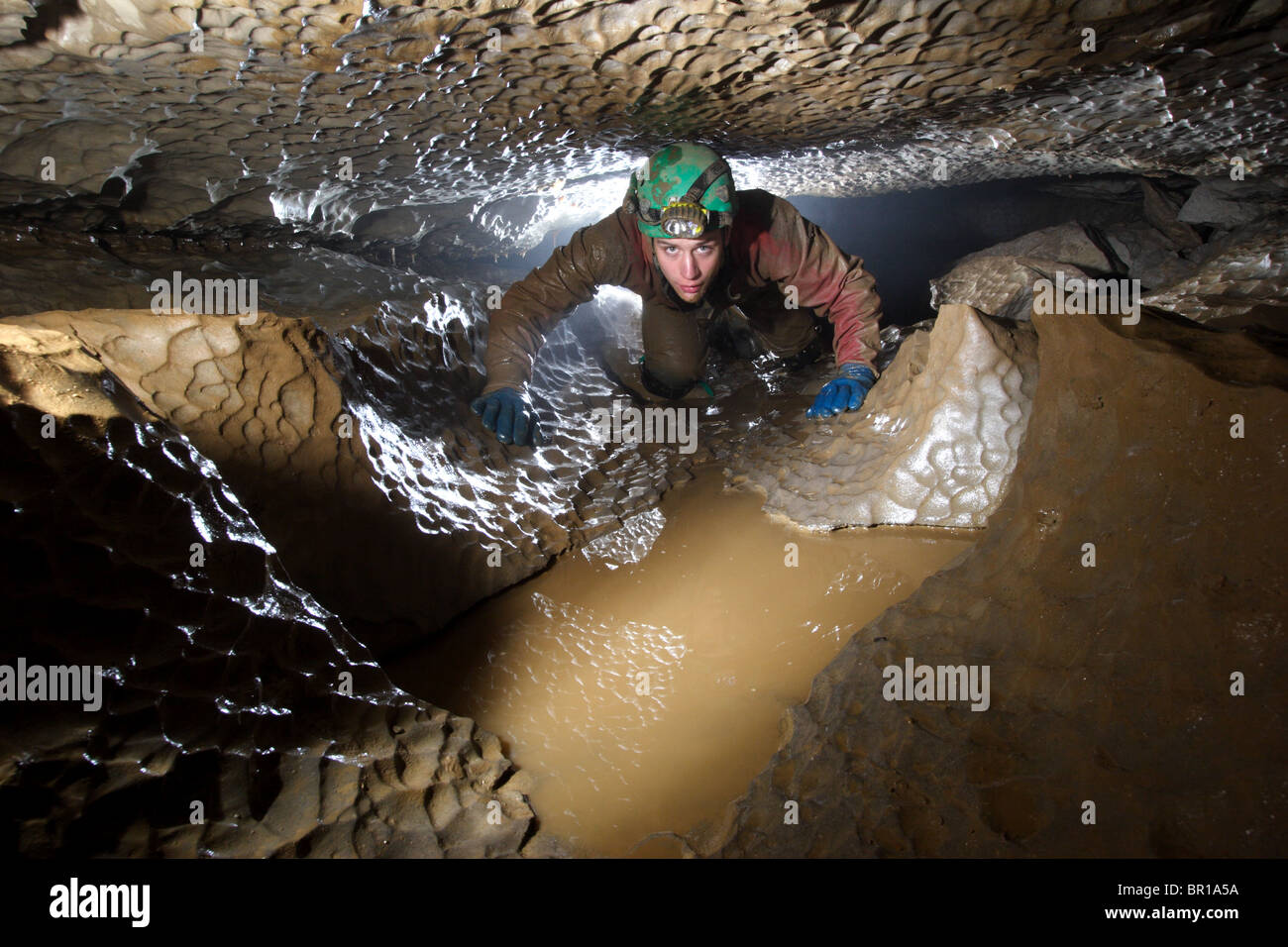 Cave explorer crawls through a low section of cave passage underground ...