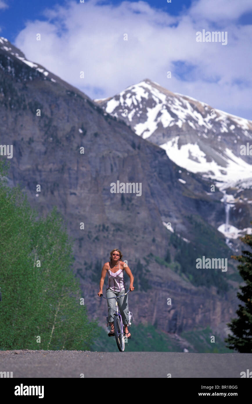 A woman rides an old bicycle with mountains in the background in ...