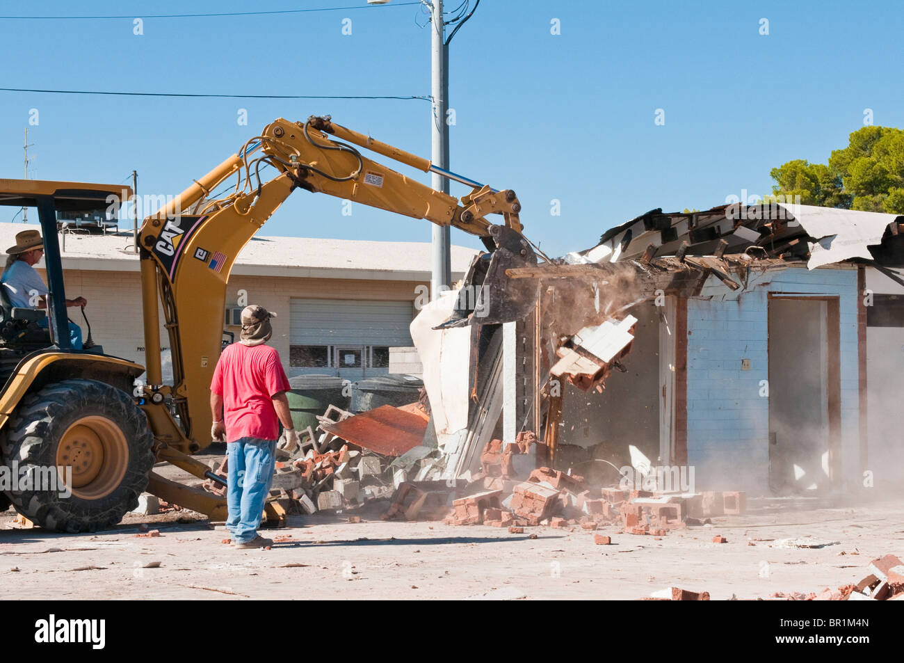 A backhoe is being used to knock down an old commercial building and ...