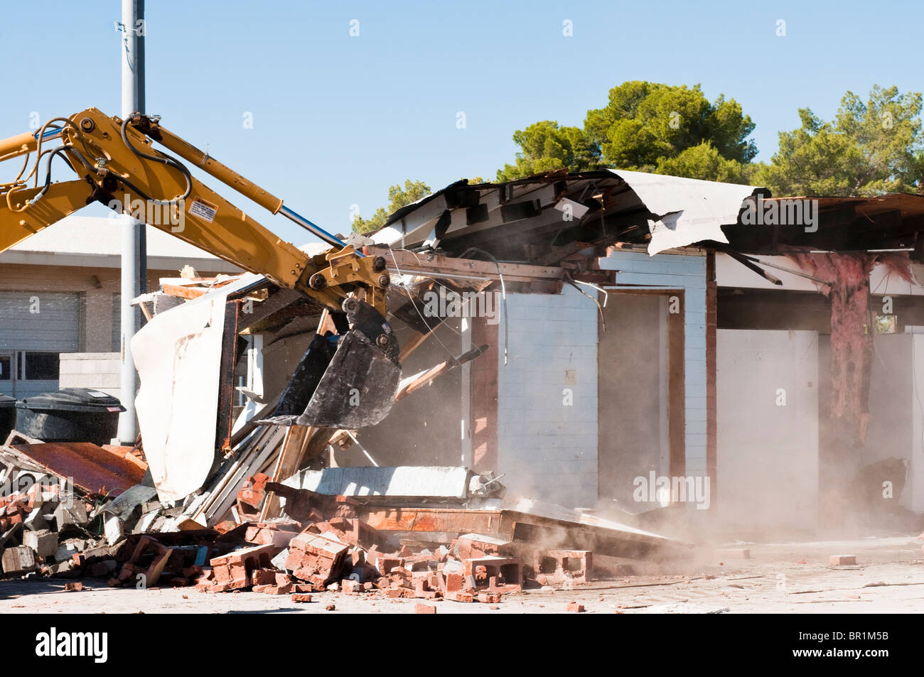 A backhoe is being used to knock down an old commercial building and ...