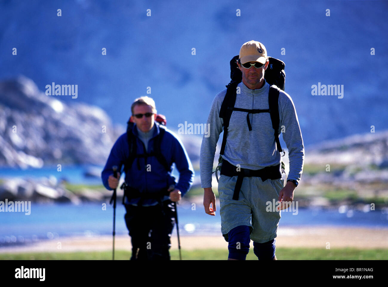 Two men backpacking in an alpine meadow with a lake in eastern Sierra ...