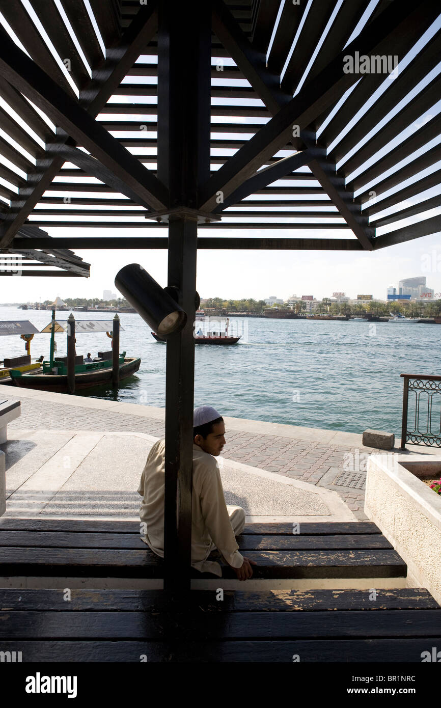 A young Muslim guy seats on a bench at the shadow by the Creek in Dubai ...