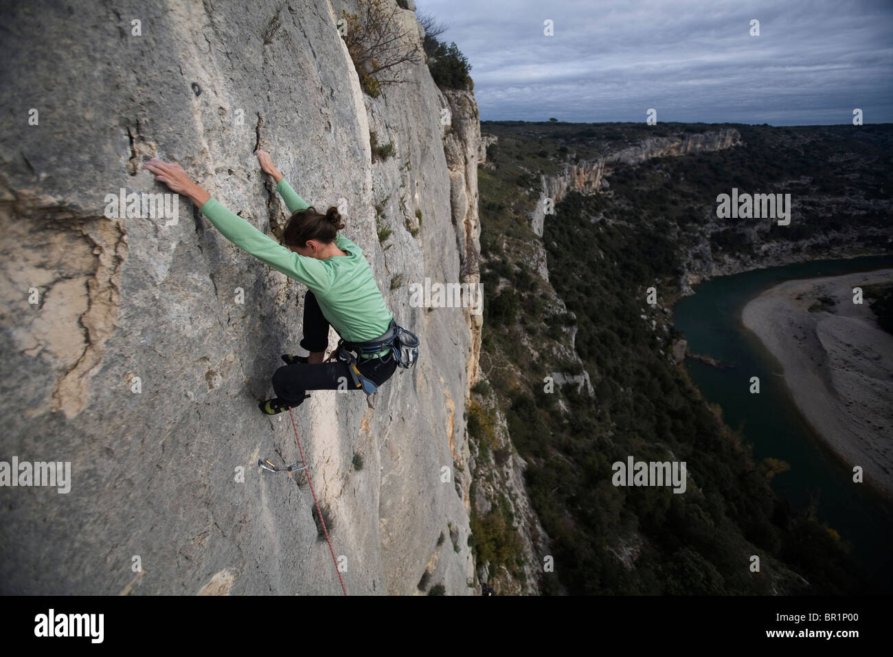 Women wearing a green shirt hangs by her fingers on cliff face above a ...