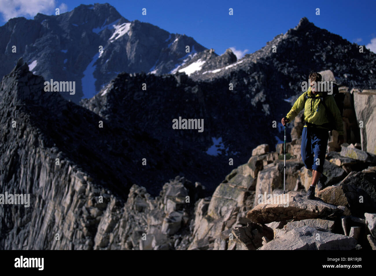 A man hiking along a boulder covered ridge line at Kearsarge Pass in ...