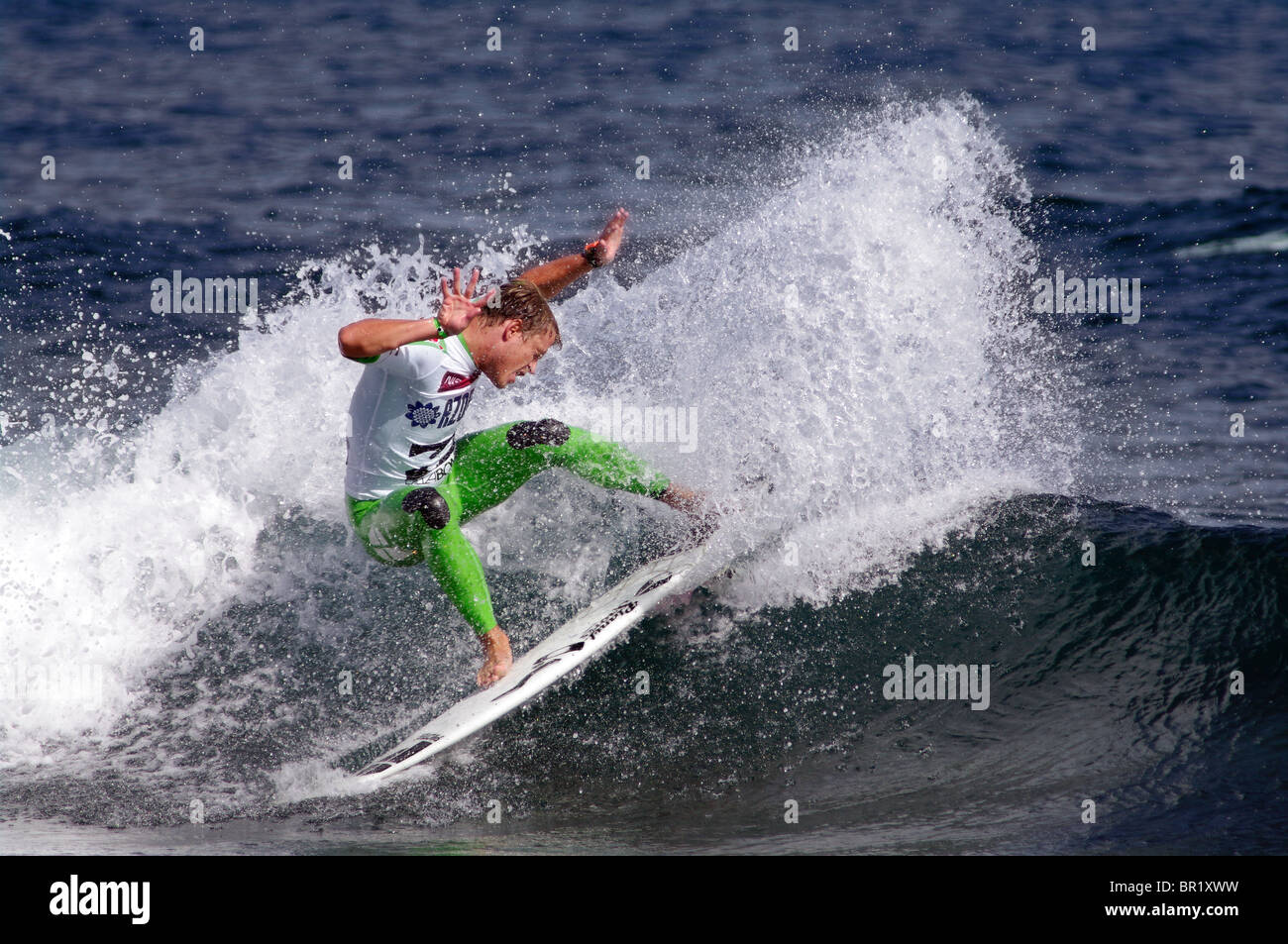A male surfer in a yellow jersey rides a wave during a surf competition ...