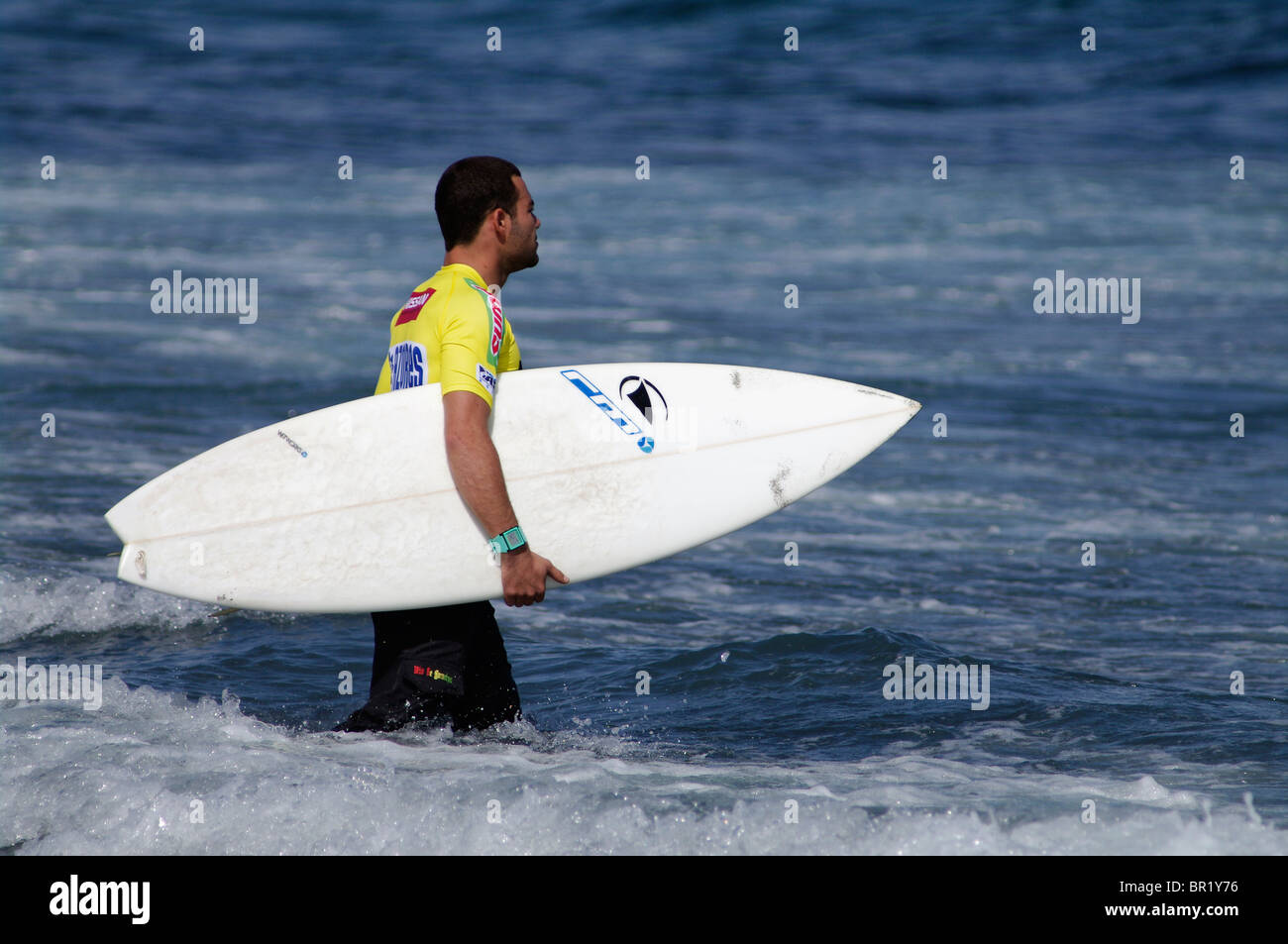 A male surfer in a yellow jersey rides a wave during a surf competition ...