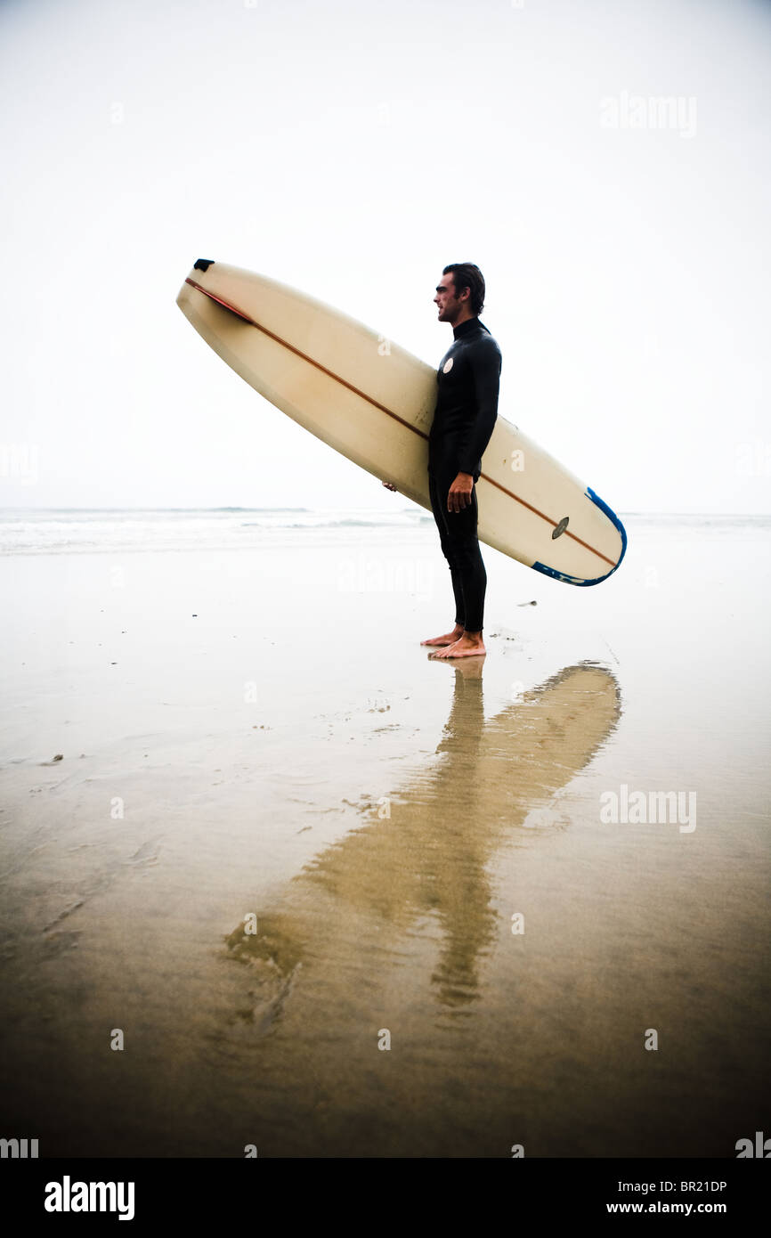 A portrait of a surfer standing on the beach with a reflection in the ...