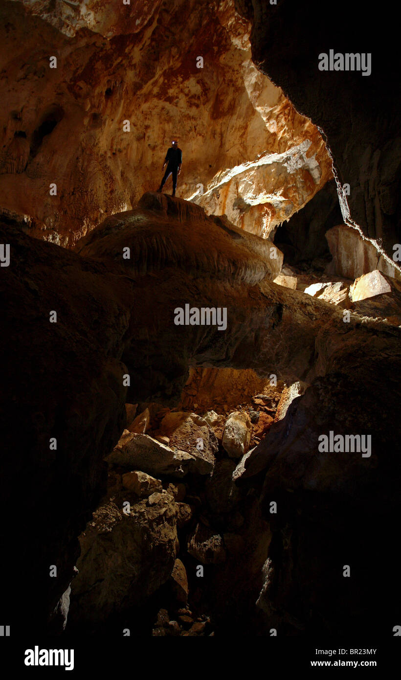 A lone cave explorer stands on top of a rock bridge in a large boulder ...