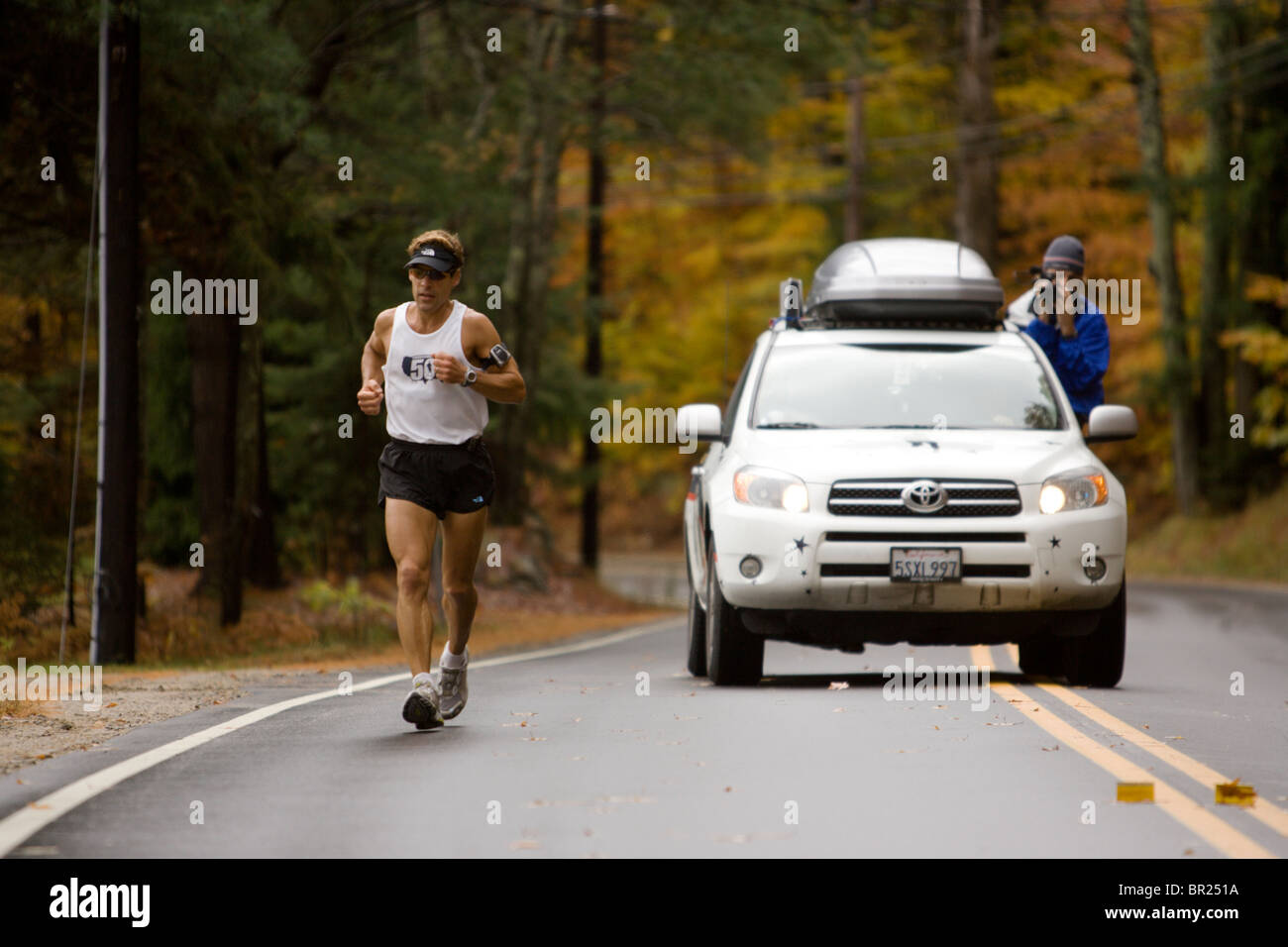 Man running a marathon and being videotaped/documented by a support car ...