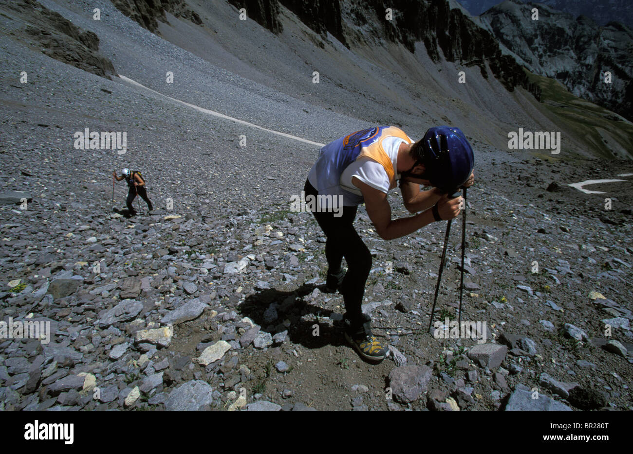 Exhausted racer leaning over trekking poles at the top of a hike in an ...