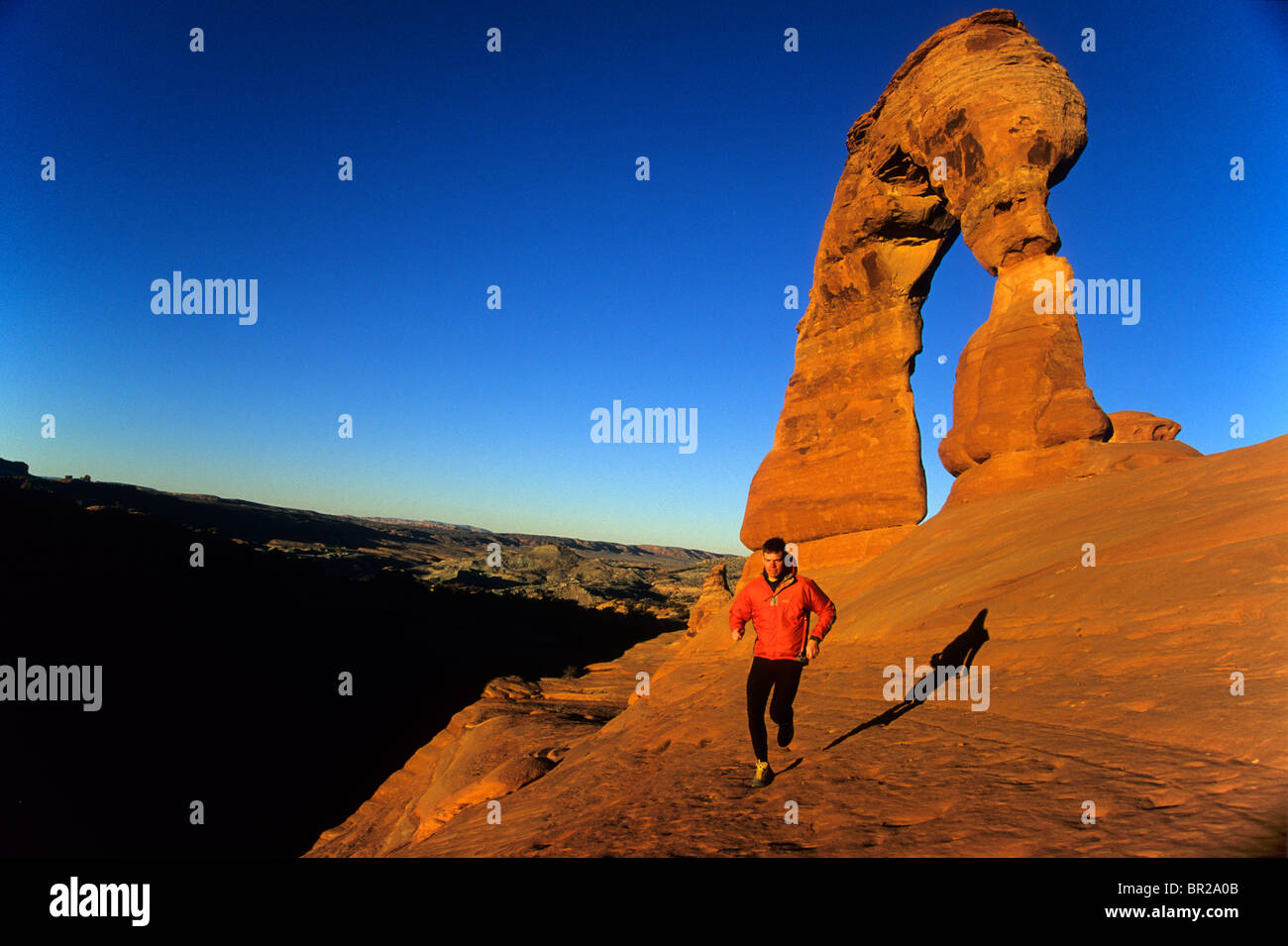 Man running beneath Delicate Arch with moon visibla through arch ...