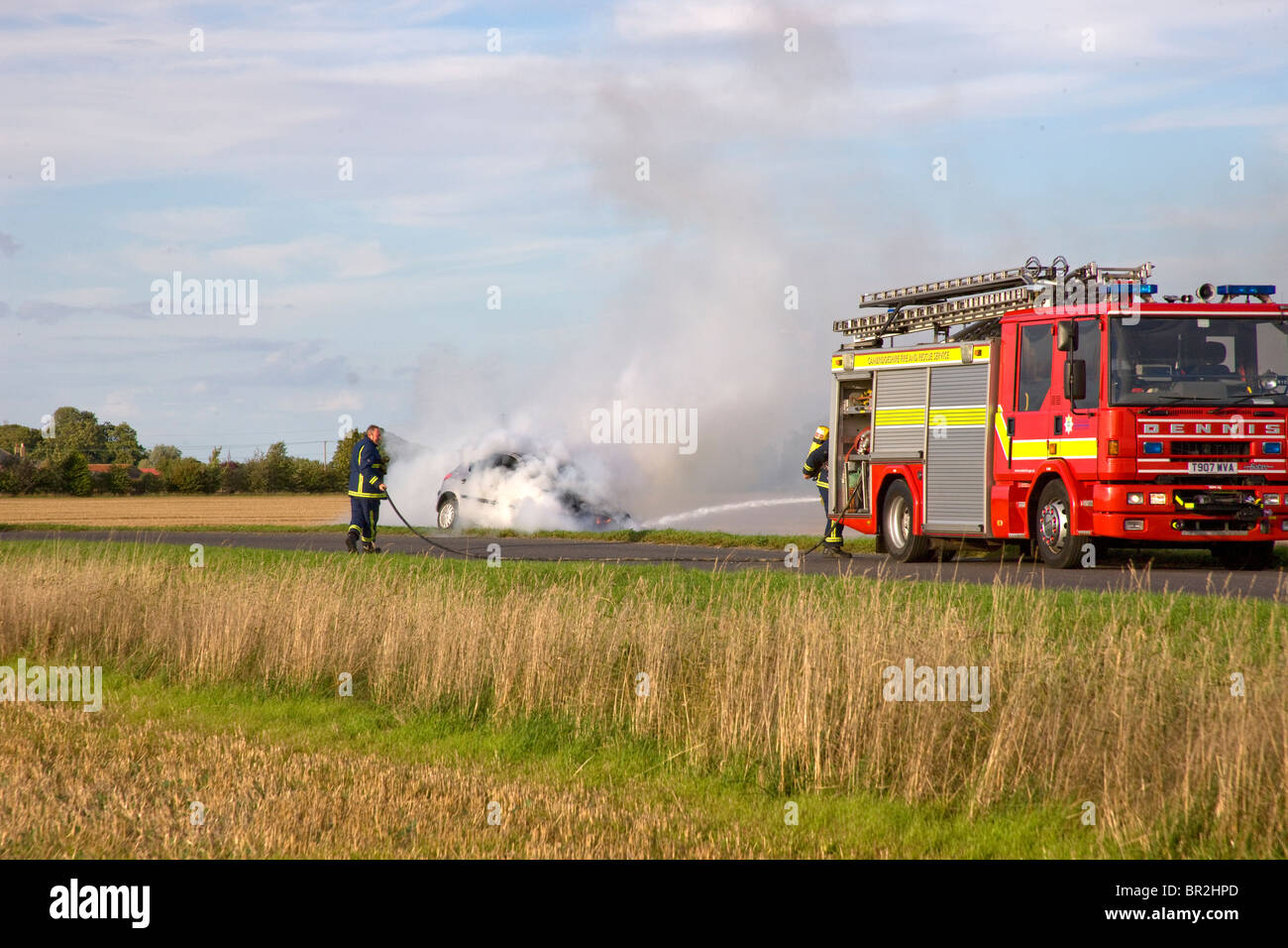 Car on roadside verge with it's engine on fire. The Fire Brigade having ...