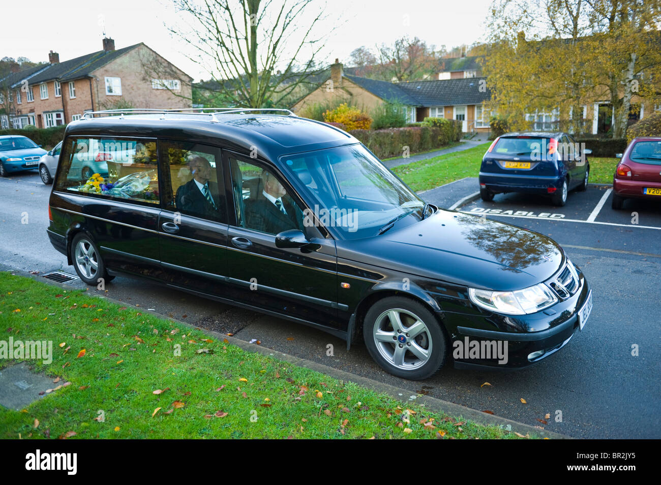 Funeral, black hearse with undertaker leaving housing estate in Welwyn ...