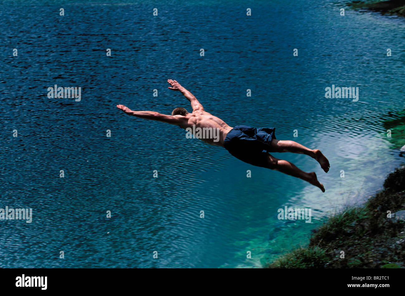 Man swan diving into a turquoise alpine lake Stock Photo - Alamy