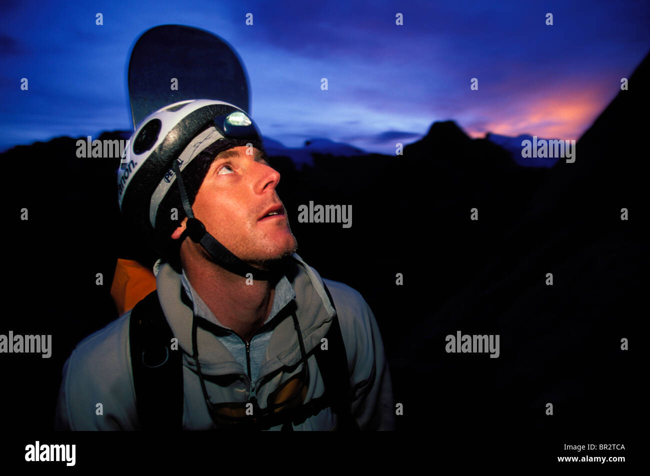 Headshot of a man climbing at night with a snowboard on his back Stock ...