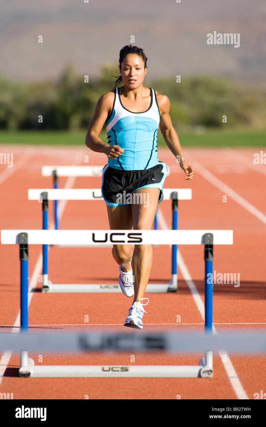 Attractive woman running hurdles on a track Stock Photo - Alamy