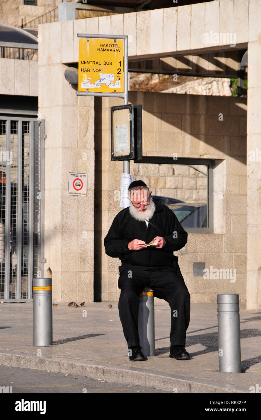 Orthodox Jew with prayer book waiting at a bus stop, Jerusalem, Israel ...