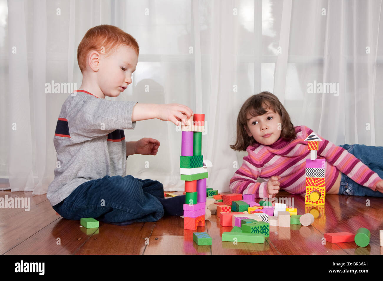 Two kids playing with wooden blocks on polished floor with window ...