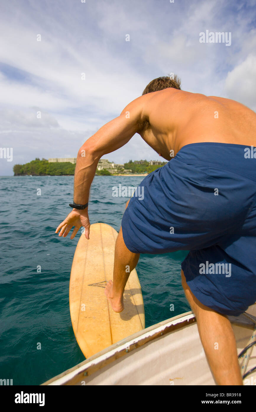 A man steps off a boat onto a surfoard in Hanalei Bay, Kauai, Hawaii ...