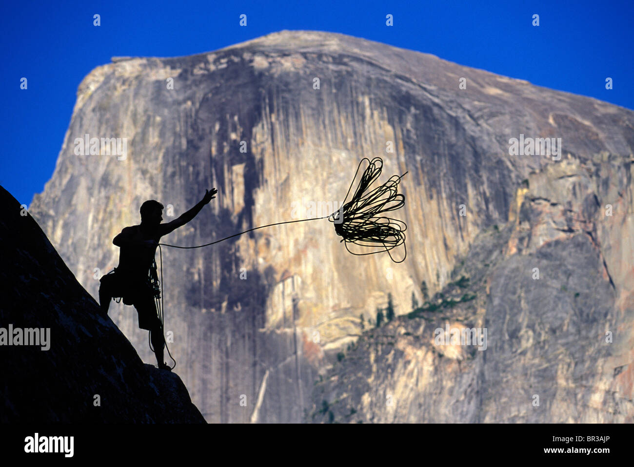 Silhouette against a granite dome of a climber throwing a rope off a ...