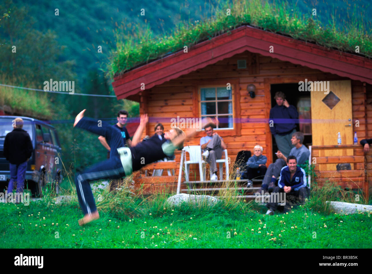 Man falling from a slackline in front of grass covered cabin and ...
