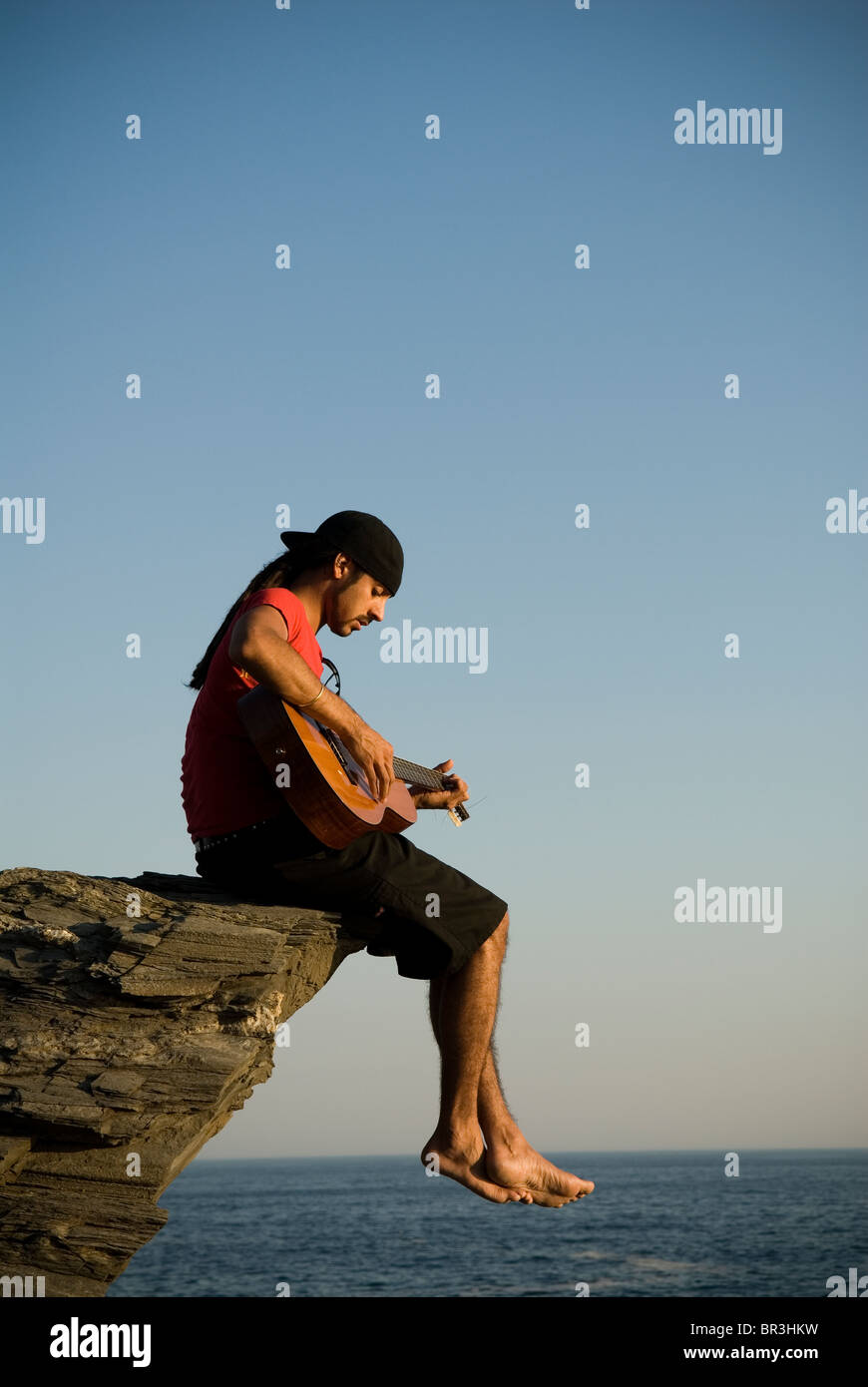 Man playing guitar on cliff above ocean Stock Photo - Alamy